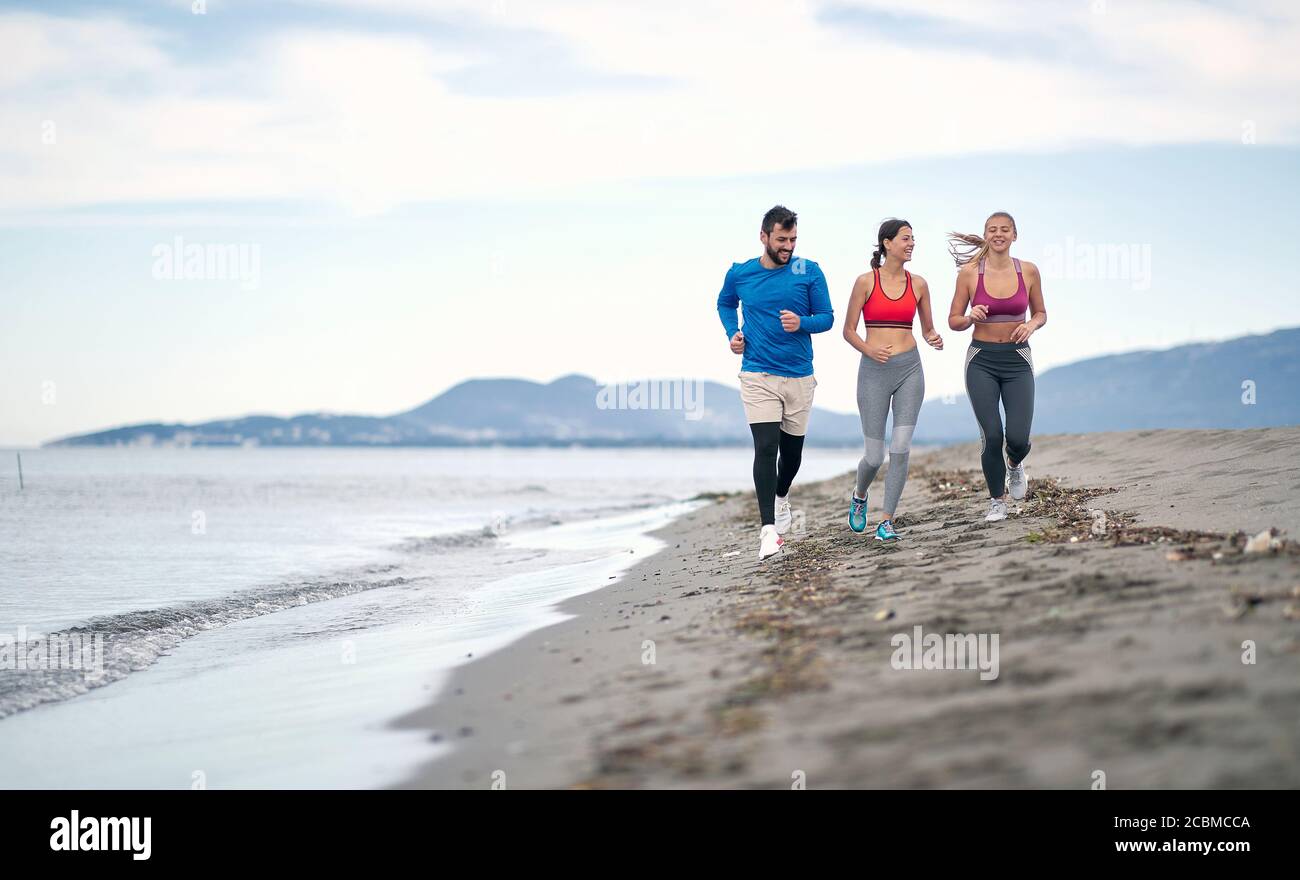 Group of three people jogging together on the beach Stock Photo - Alamy