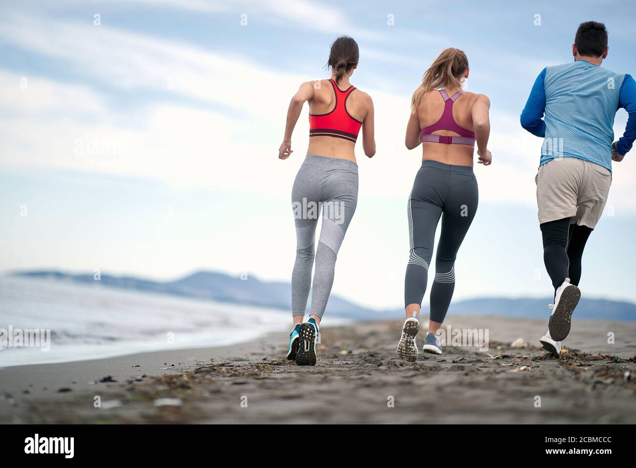 Group of three people jogging together on the beach Stock Photo - Alamy
