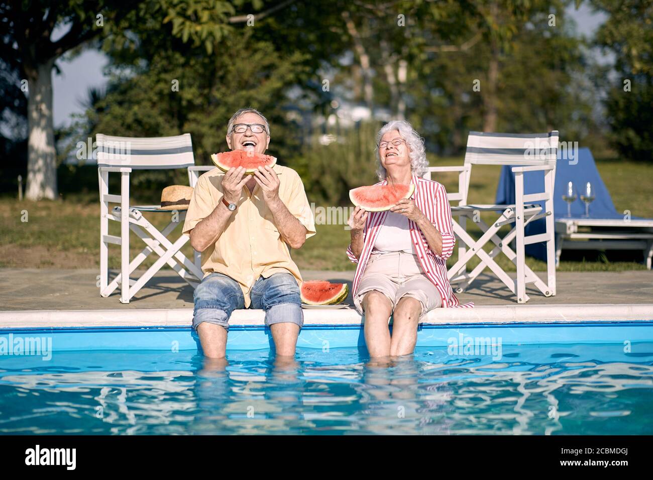 Elderly couple eating watermelon by the pool.Happy man and woman enjoy ...