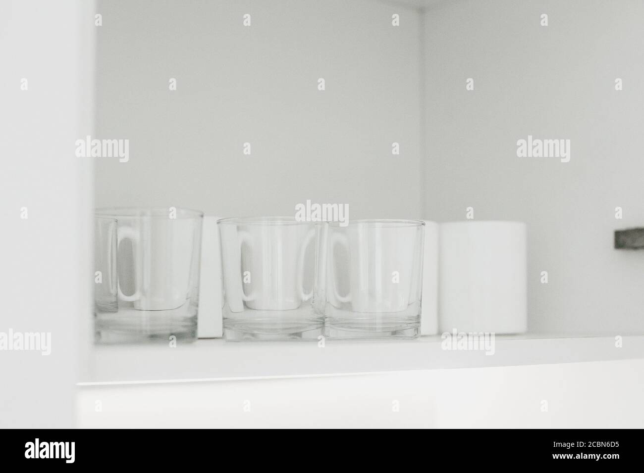 Transparent glasses and white ceramic cups on white shelf in modern ...