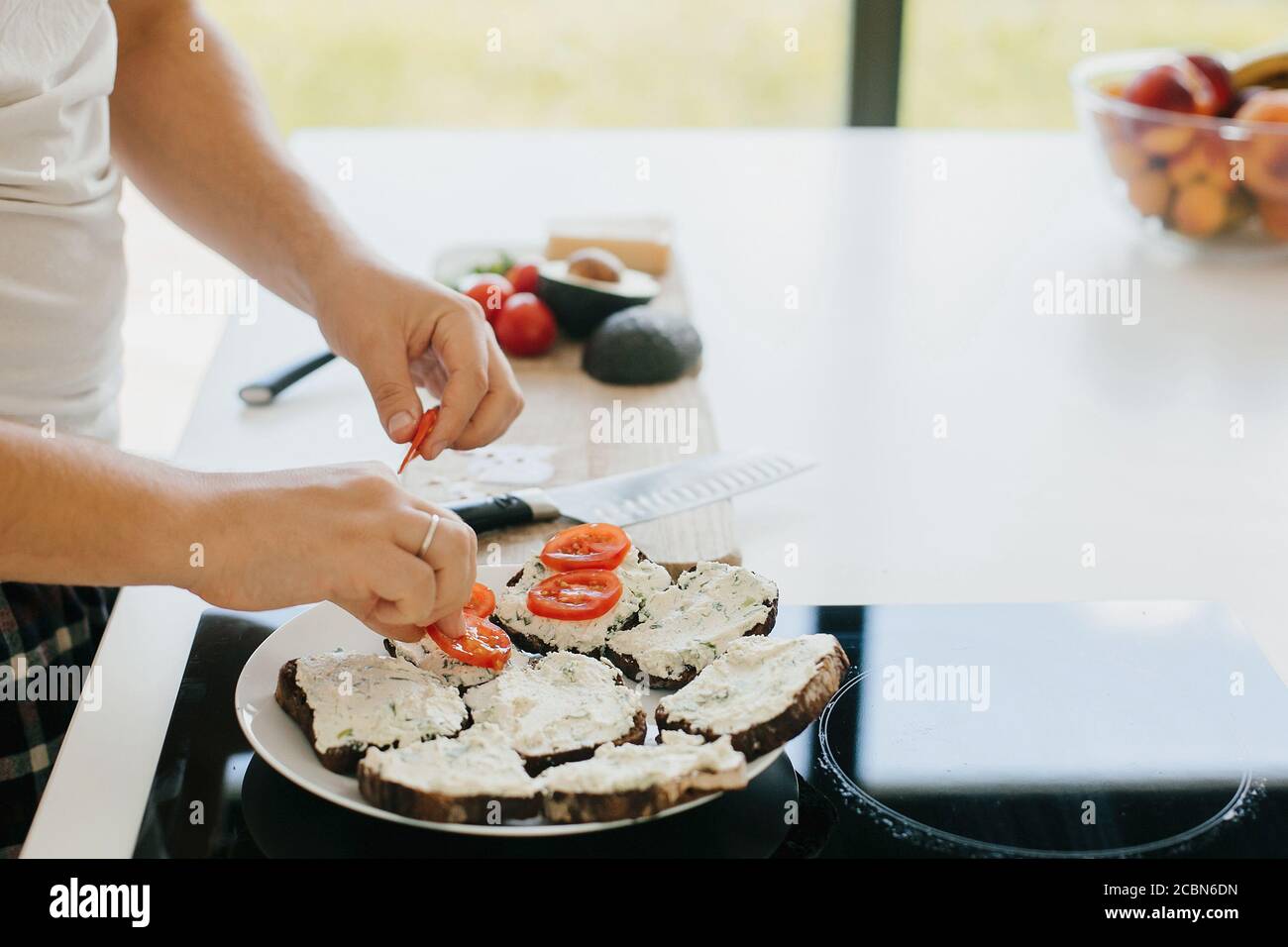 Person putting tomato slice on cheese cream on whole grain bread on ...