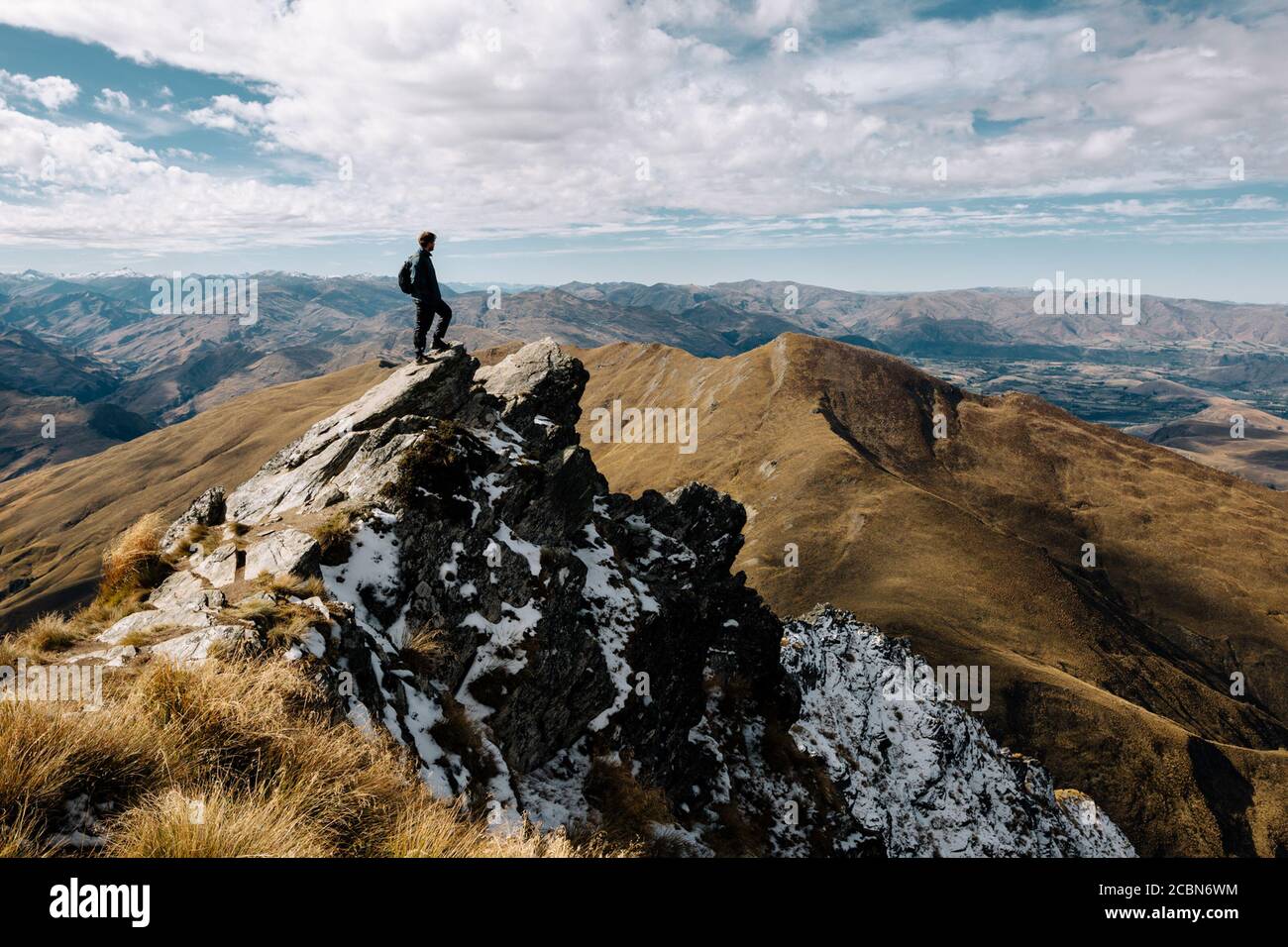 Mesmerizing shot of a male standing on a top of the mountain at daytime ...