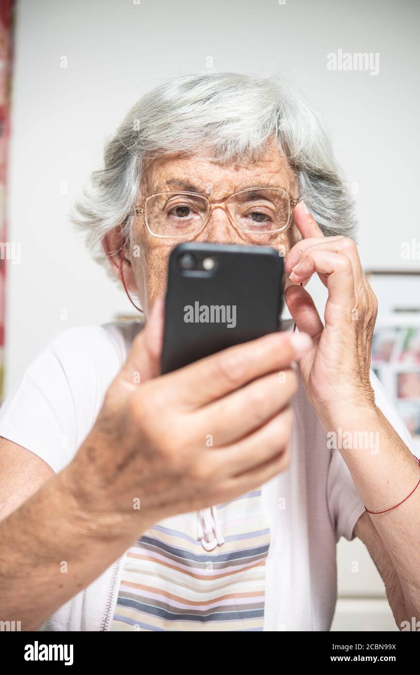 An elder lady reading something on the smartphone looking confused ...