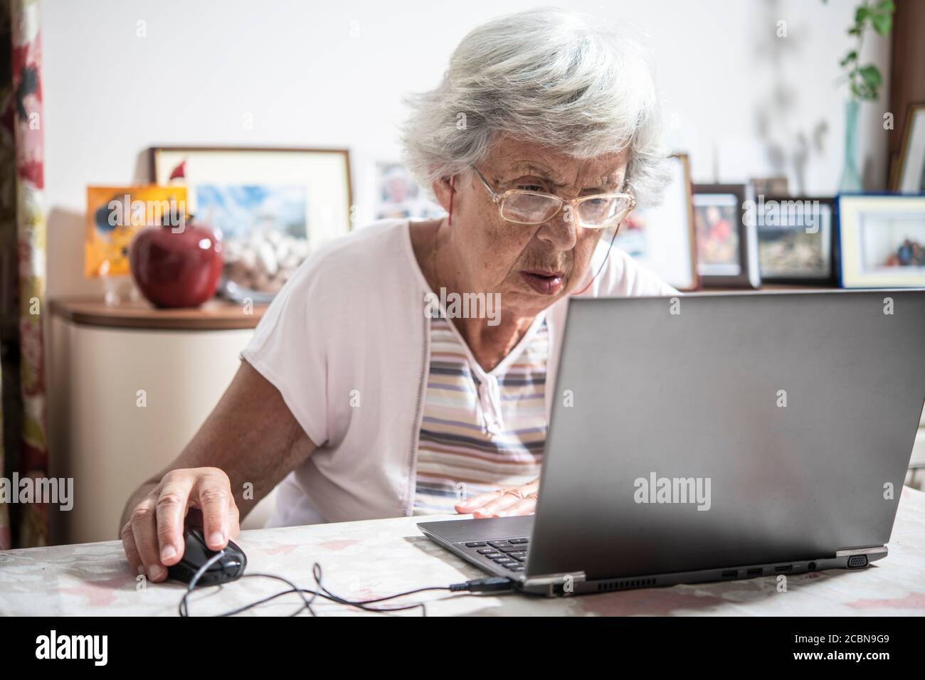 An elder lady with glasses staring at laptop's monitor while clicking ...