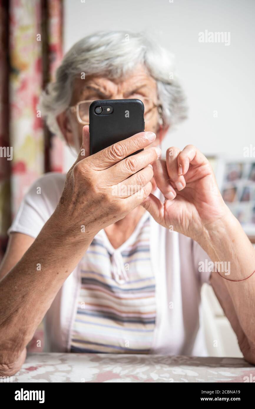 An elder lady with glasses staring at smartphone's screen while holding ...
