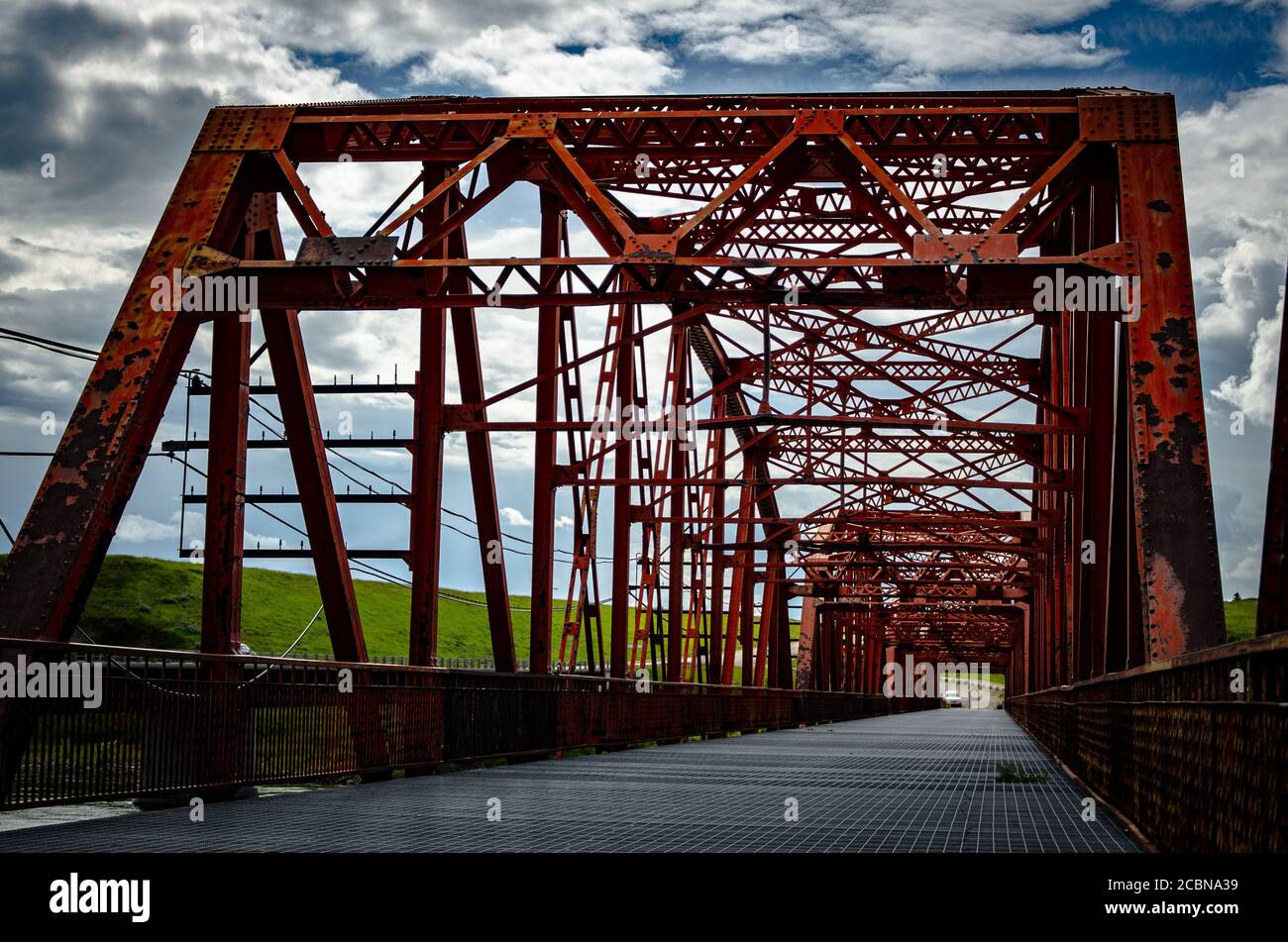 View of a red iron bridge crossing a river with roadway on a cloudy day ...