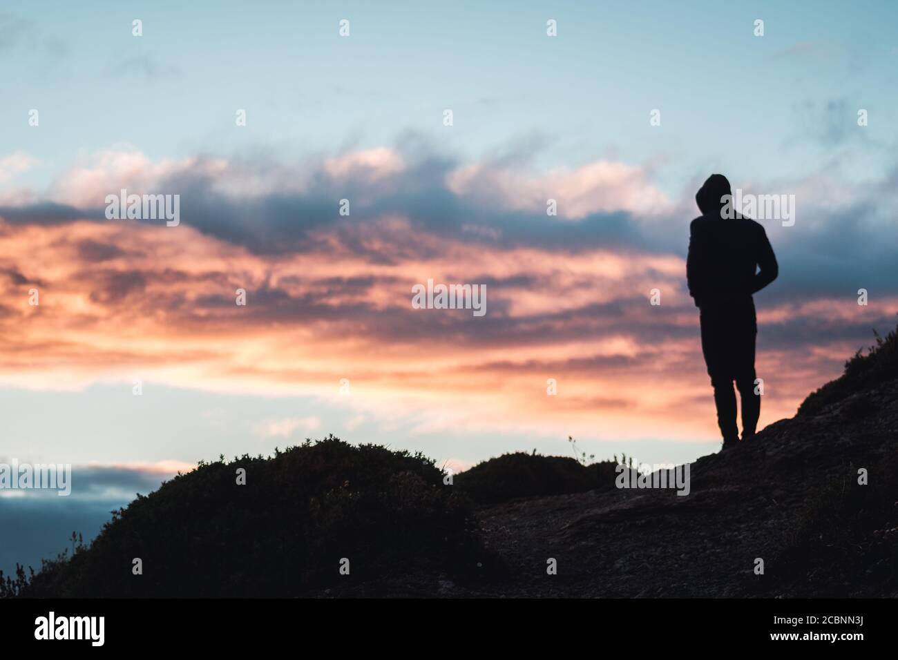 Lonely person standing on a hill looking at the sunset clouds ...