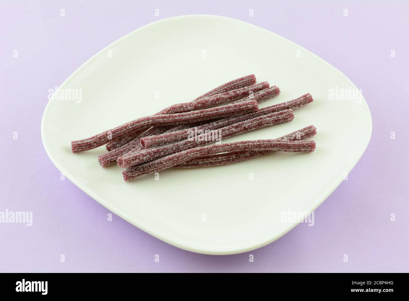 Sour blueberry candy sticks on white snack plate on lavender background ...