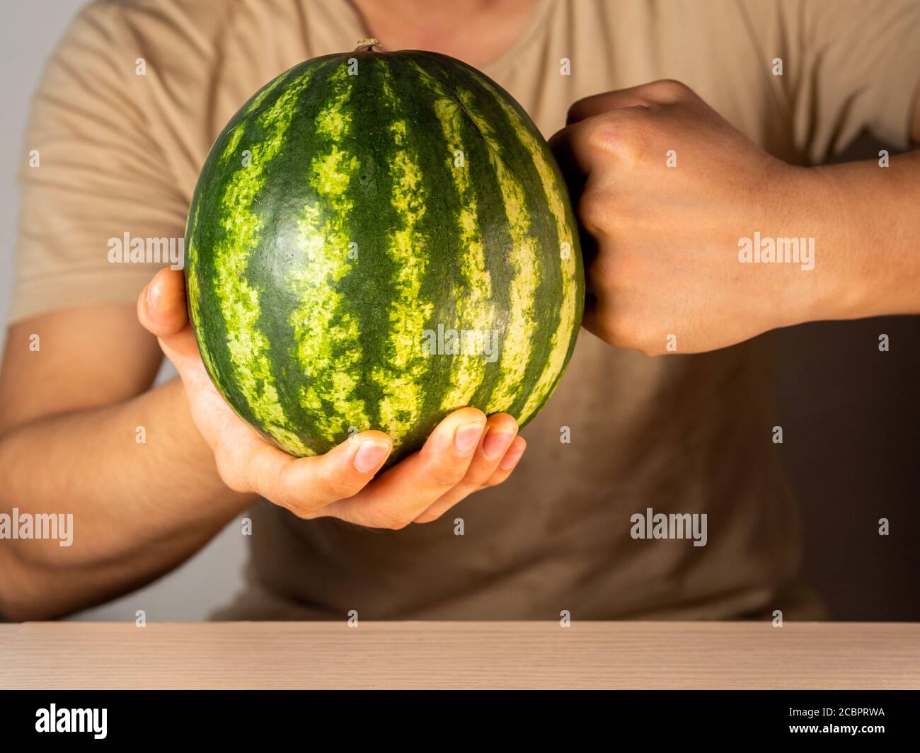 Male hand holding a watermelon from one side and making a fist from the ...