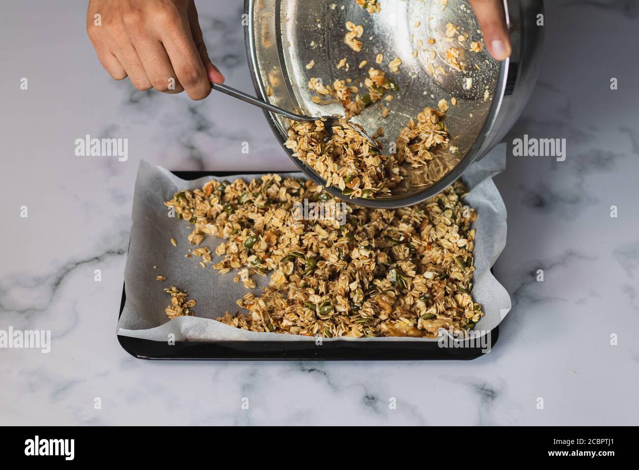 Closeup shot of a chef pouring out an oat and nut mixture onto an oven ...