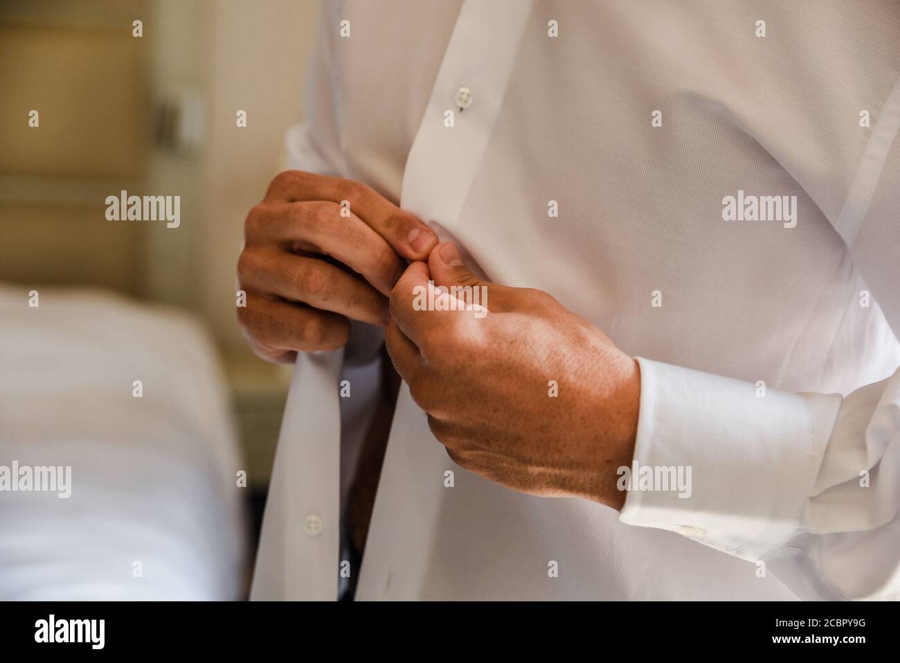 Elegant man buttoning up his white shirt Stock Photo - Alamy