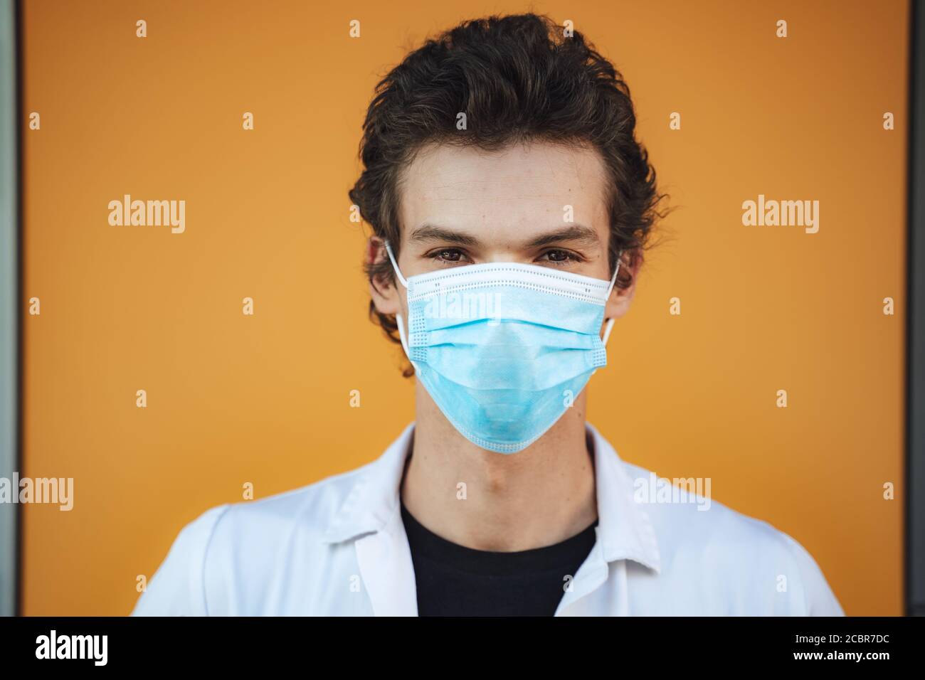 Close up portrait of young male doctor wearing face mask against yellow ...