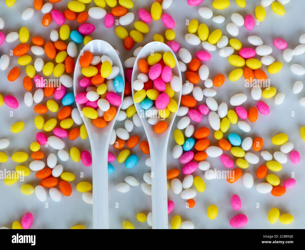 Multi colored fennel sugar candy in spoons and scattered as background ...