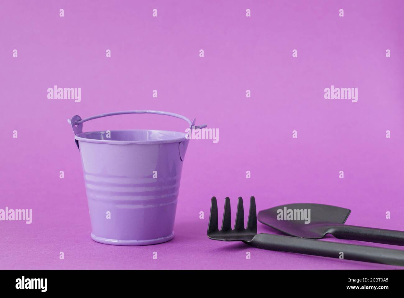Toy iron bucket light purple, rake and shovel on a dark purple ...