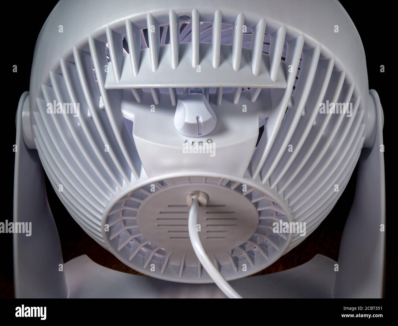 Closeup of the rear of a modern, white plastic, desktop fan, turned on ...