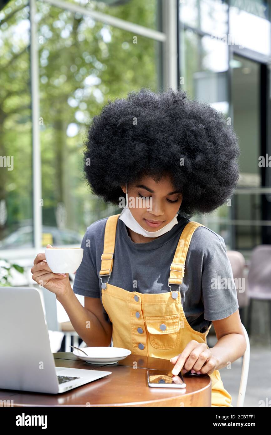African teen girl wearing face mask using phone sit at table in outdoor cafe Stock Photo - Alamy