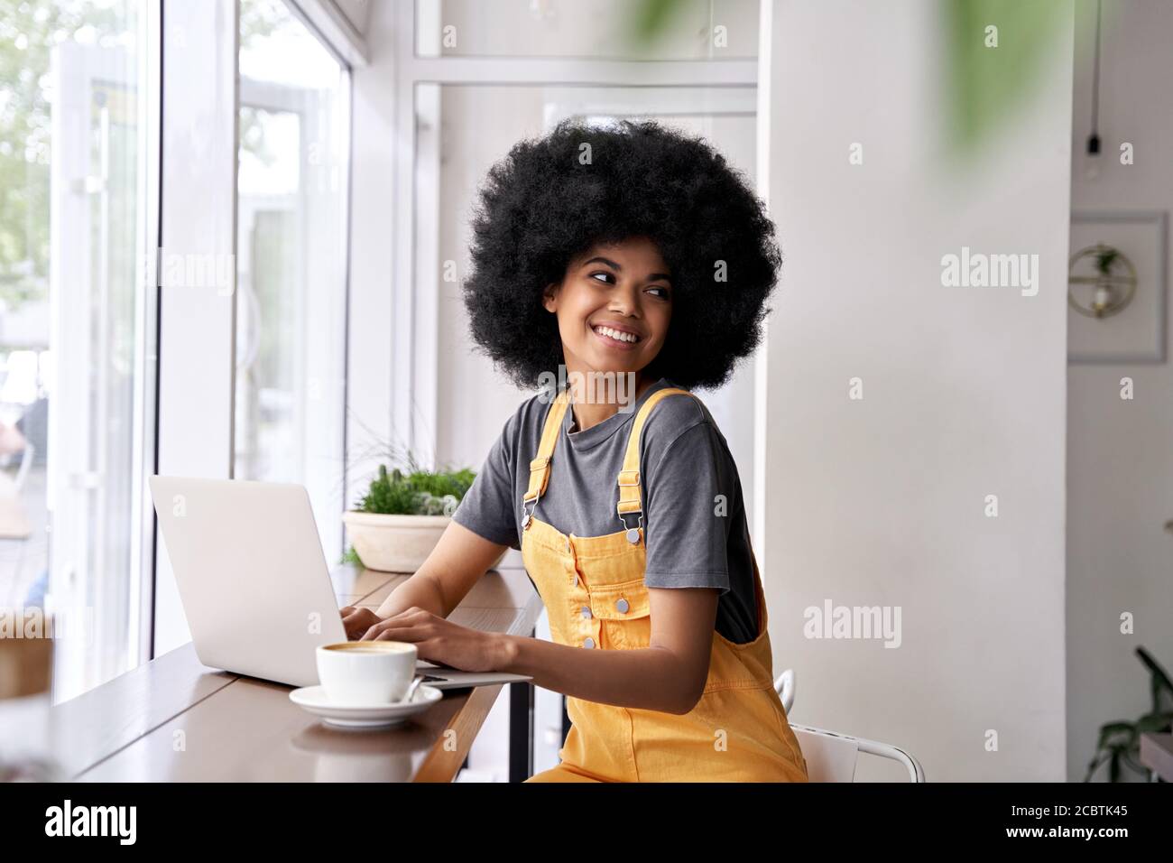 Happy African teen girl student using laptop sit at table in cafe with ...