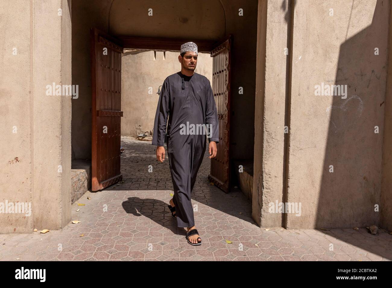 Omani man walking through one of the big entrance of Nizwa fort Stock ...