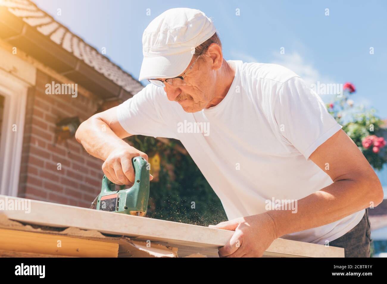 Carpenter old man using drill making holes in a wooden plank or ...