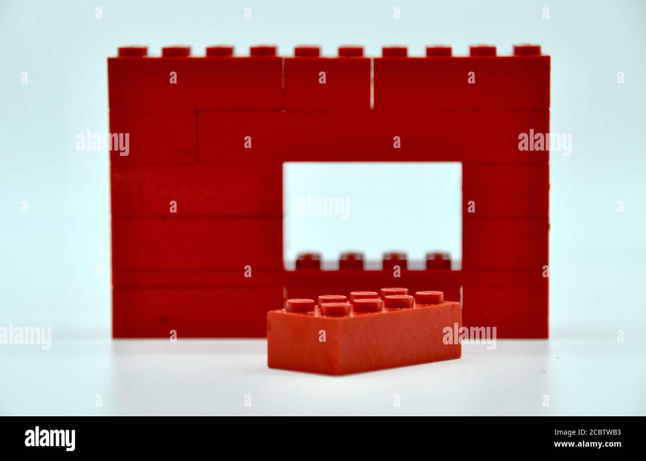 Red plastic toy brick wall with a block missing and lying in front in a ...