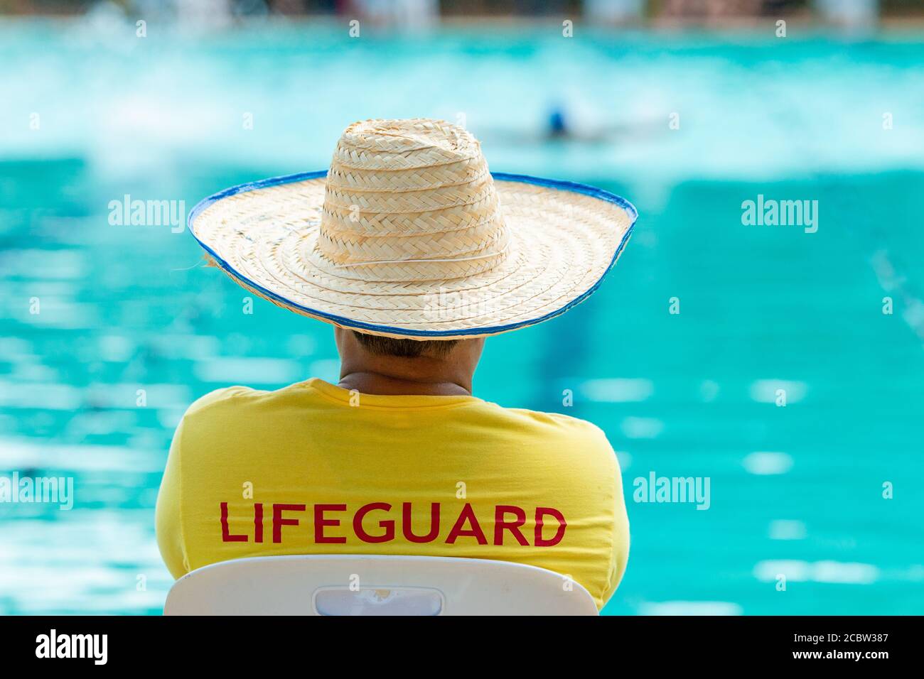 Swimming pool lifeguard man in yellow lifeguard shirt and straw hat on ...