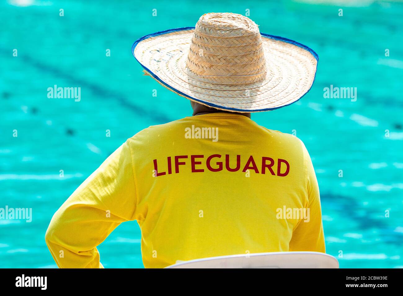 Swimming pool lifeguard man in yellow lifeguard shirt and straw hat on ...
