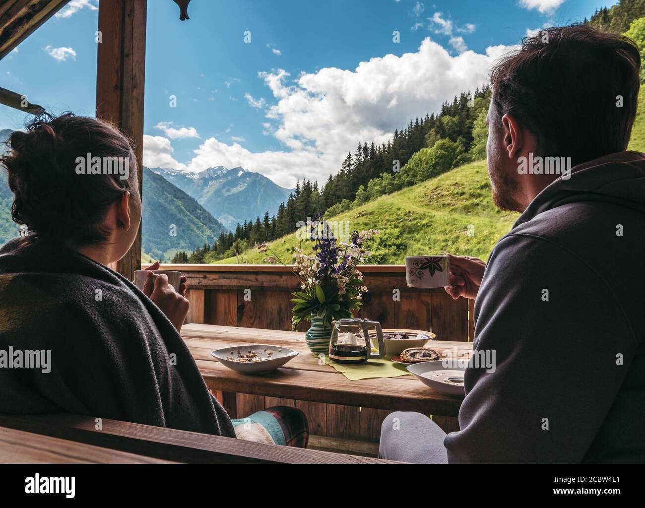 Couple sitting outside of a mountain hut, eating breakfast and enjoying ...