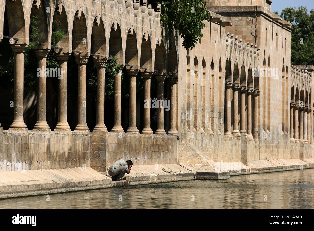 A man kneels next to Balikli Gol (Pool of Sacred Fish) also known as ...
