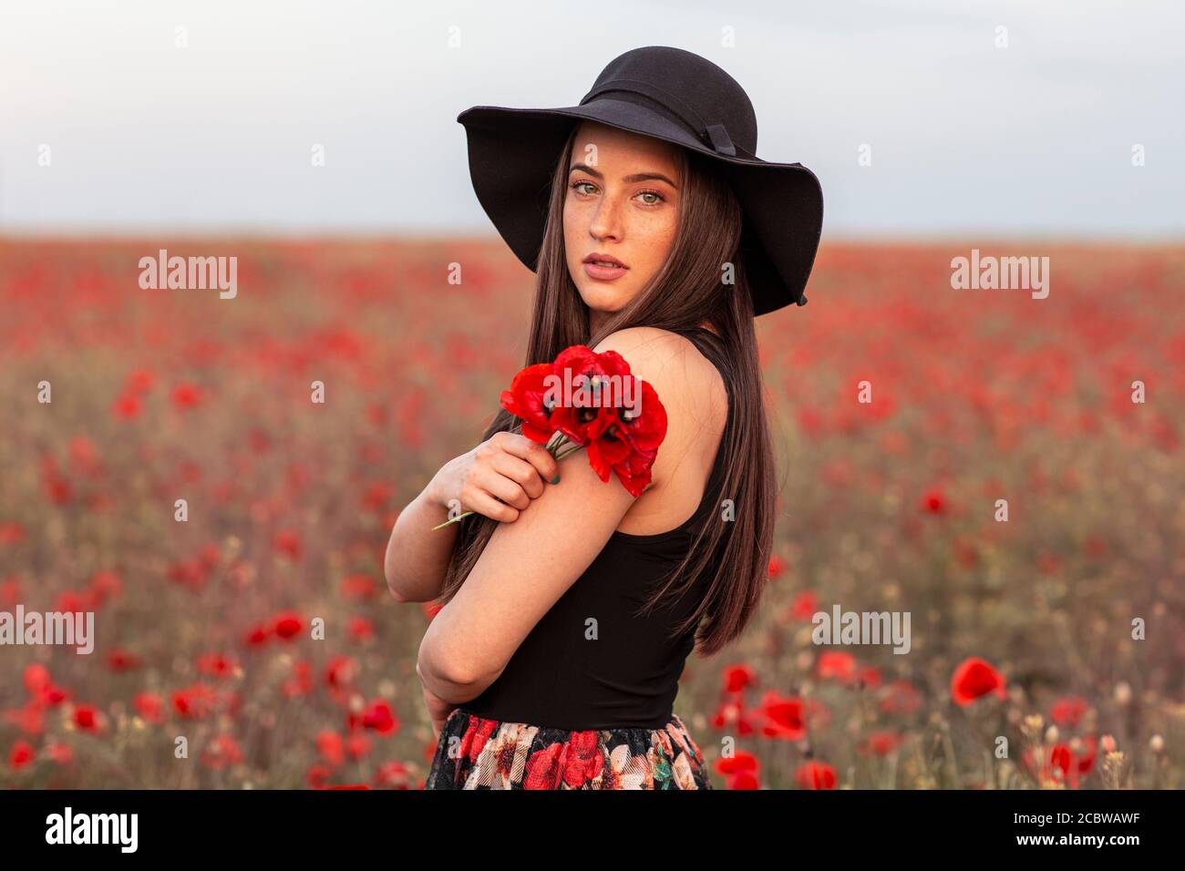 Girl at the red field with hat and flower Stock Photo - Alamy
