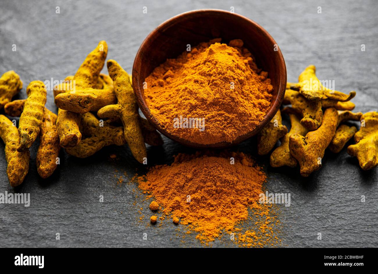 Yellow turmeric powder and dry roots on black stone background Stock ...