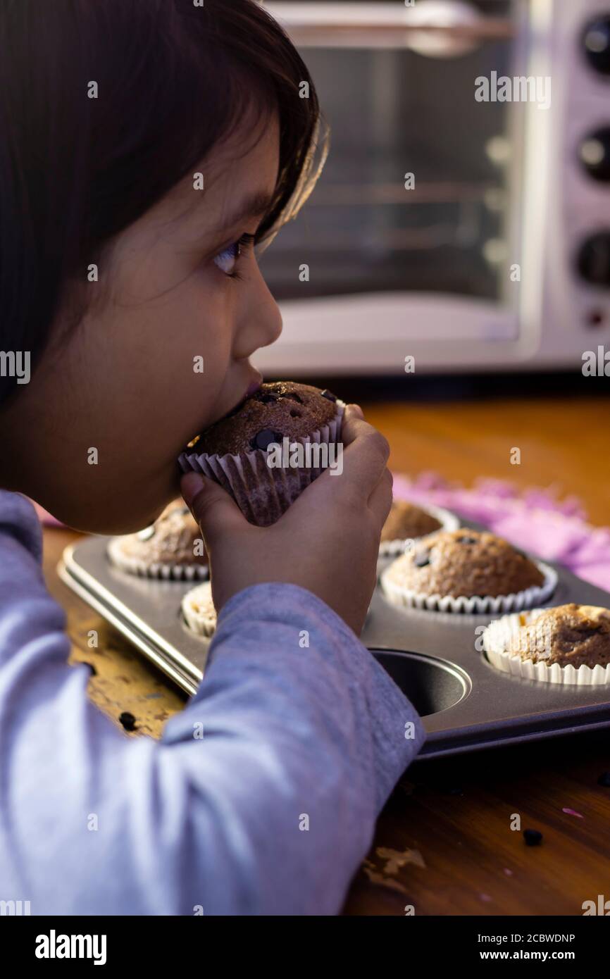 An Indian girl child eating a homemade chocolate muffin cup cake baking ...
