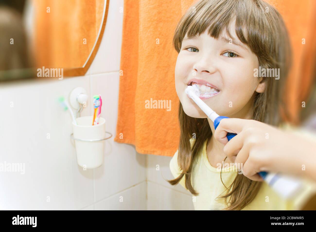 Girl brushing her teeth with toothpaste. Smiles and looks into the lens ...