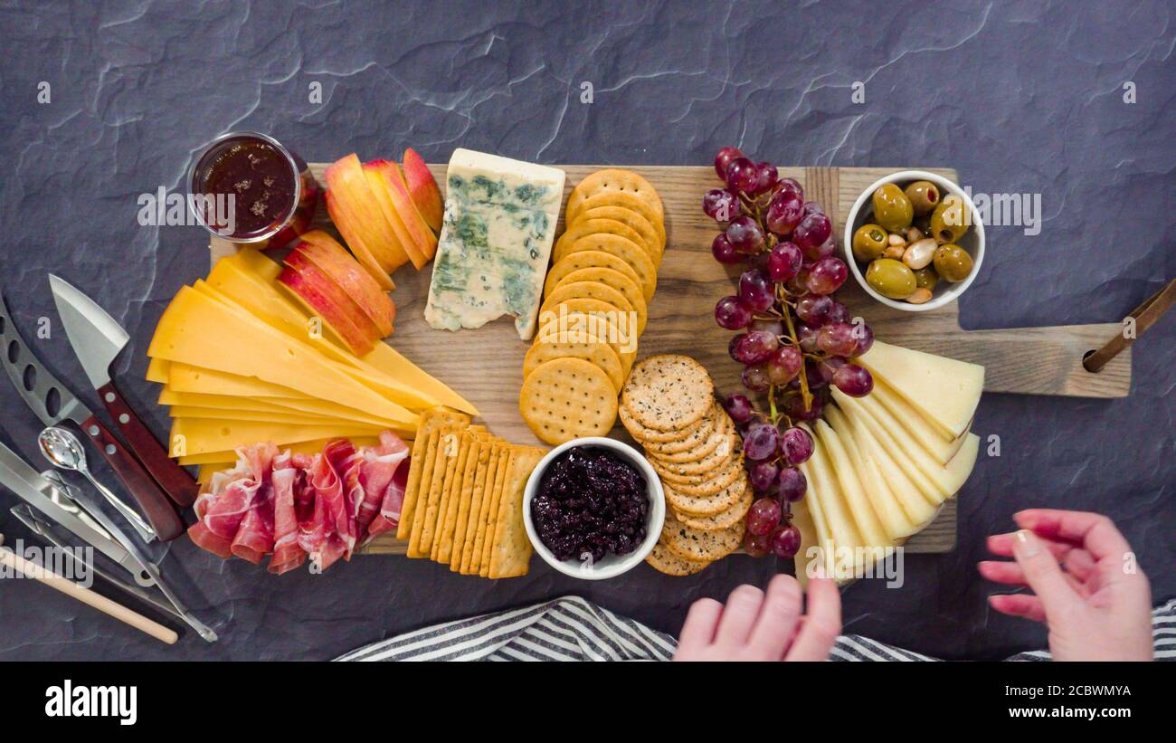 Flat lay. Arranging gourmet cheese, crakers, and fruits on a board for ...