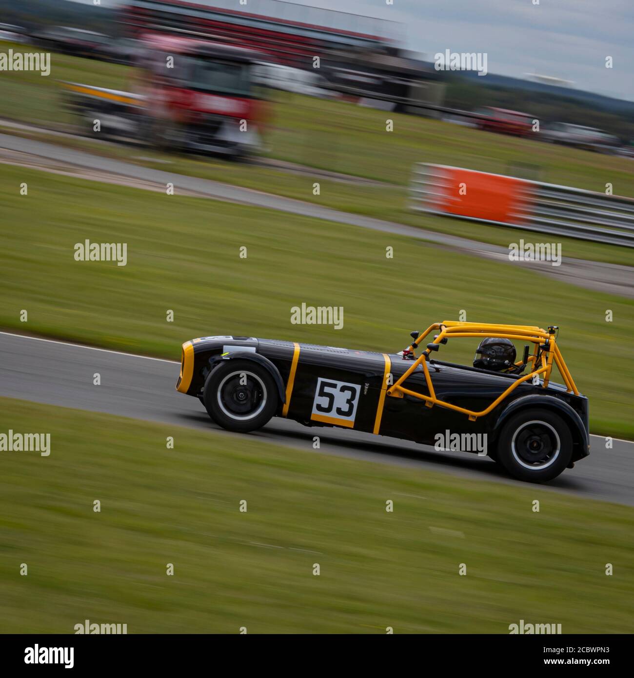 A panning shot of a black and yellow racing car as it circuits a track ...