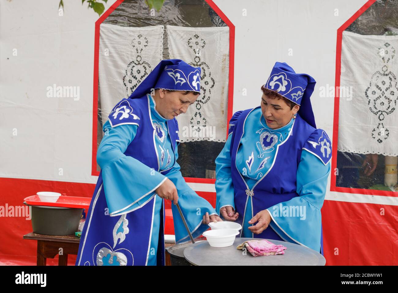 Two women in national Tatar clothes pours soup into plates for guests ...