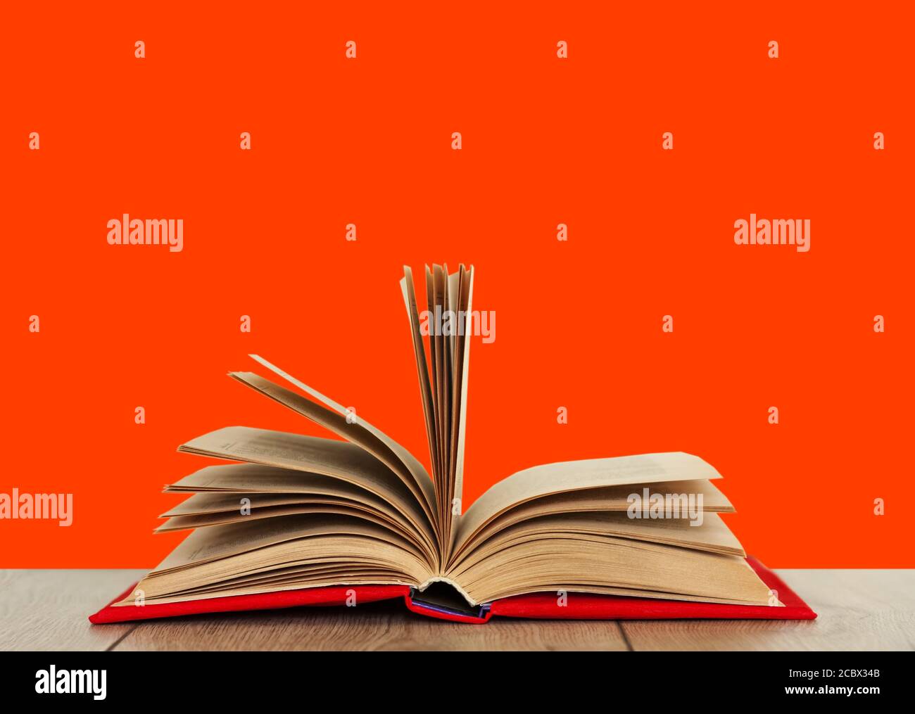 Open book textbook in a red cover on a wooden desk with orange ...
