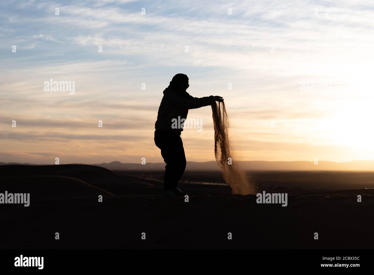Silhouette of person jumping and throwing sand in the Sahara against a ...