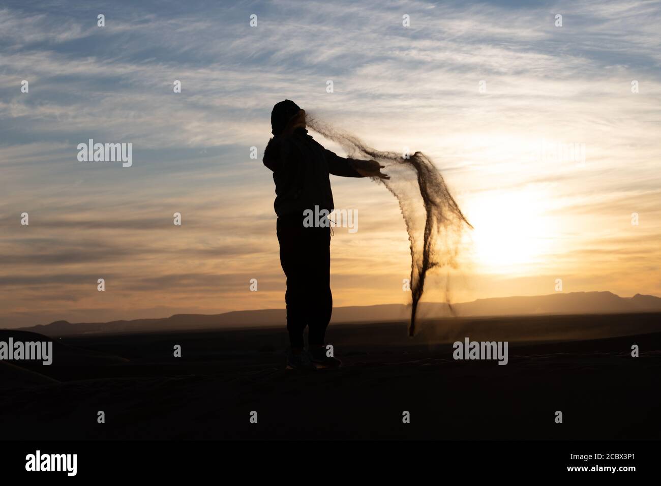 Silhouette of person jumping and throwing sand in the Sahara against a ...