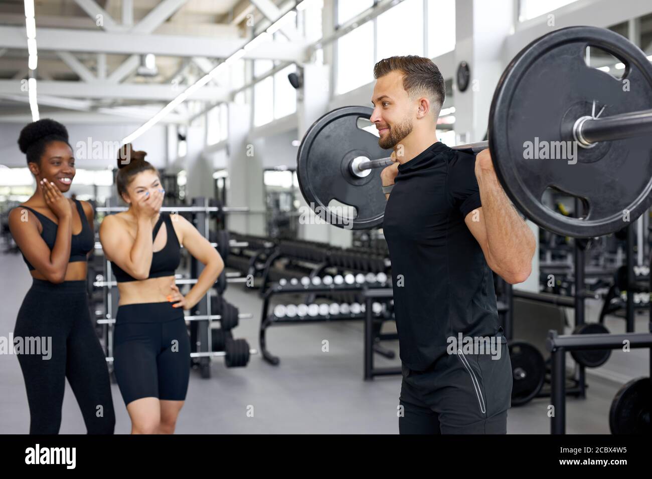 trainer shows exercises with barbell to girls in gym. diverse women ...