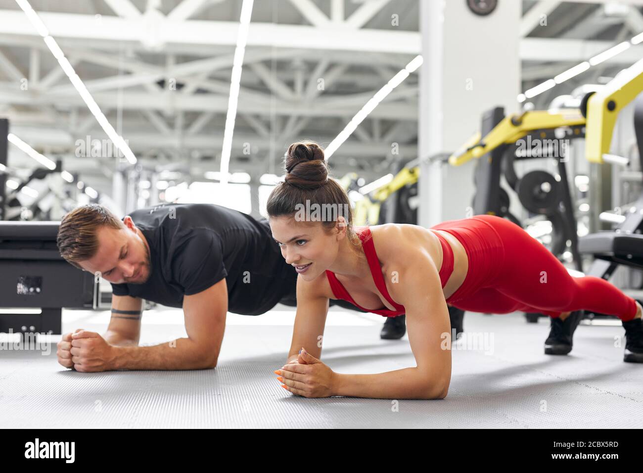 young man and woman standing in plank position at the gym, side view on ...