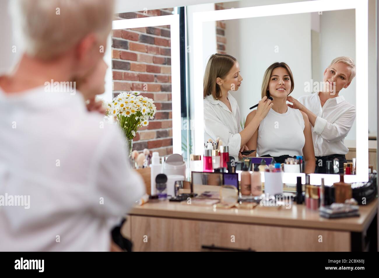two professional make-up stylists paint model's face. young caucasian ...