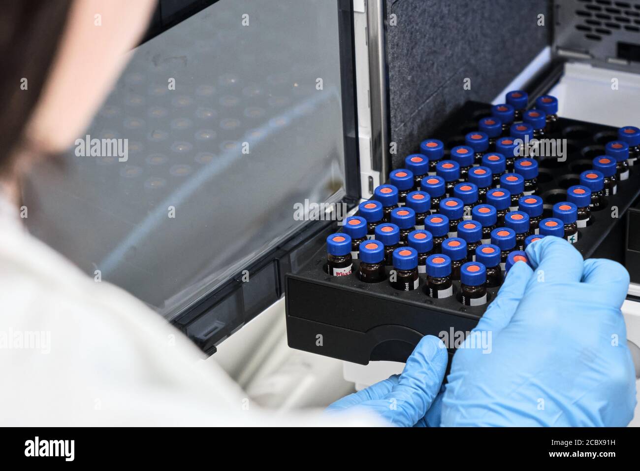 Scientist in a white lab coat putting vial with a sample into ...