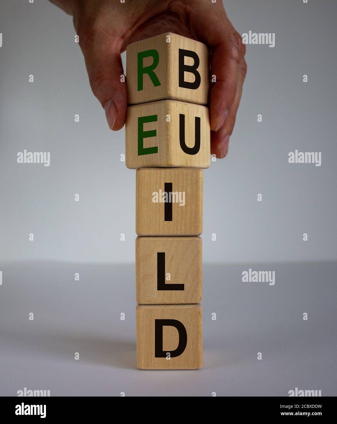 Concept word 'rebuild' on cubes on a beautiful wooden table. Male hand ...