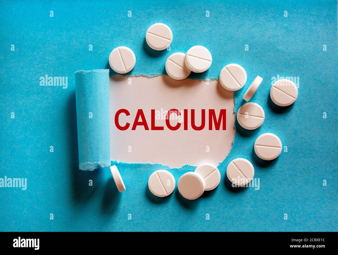 The word 'calcium' appearing behind torn blue paper. White pills ...