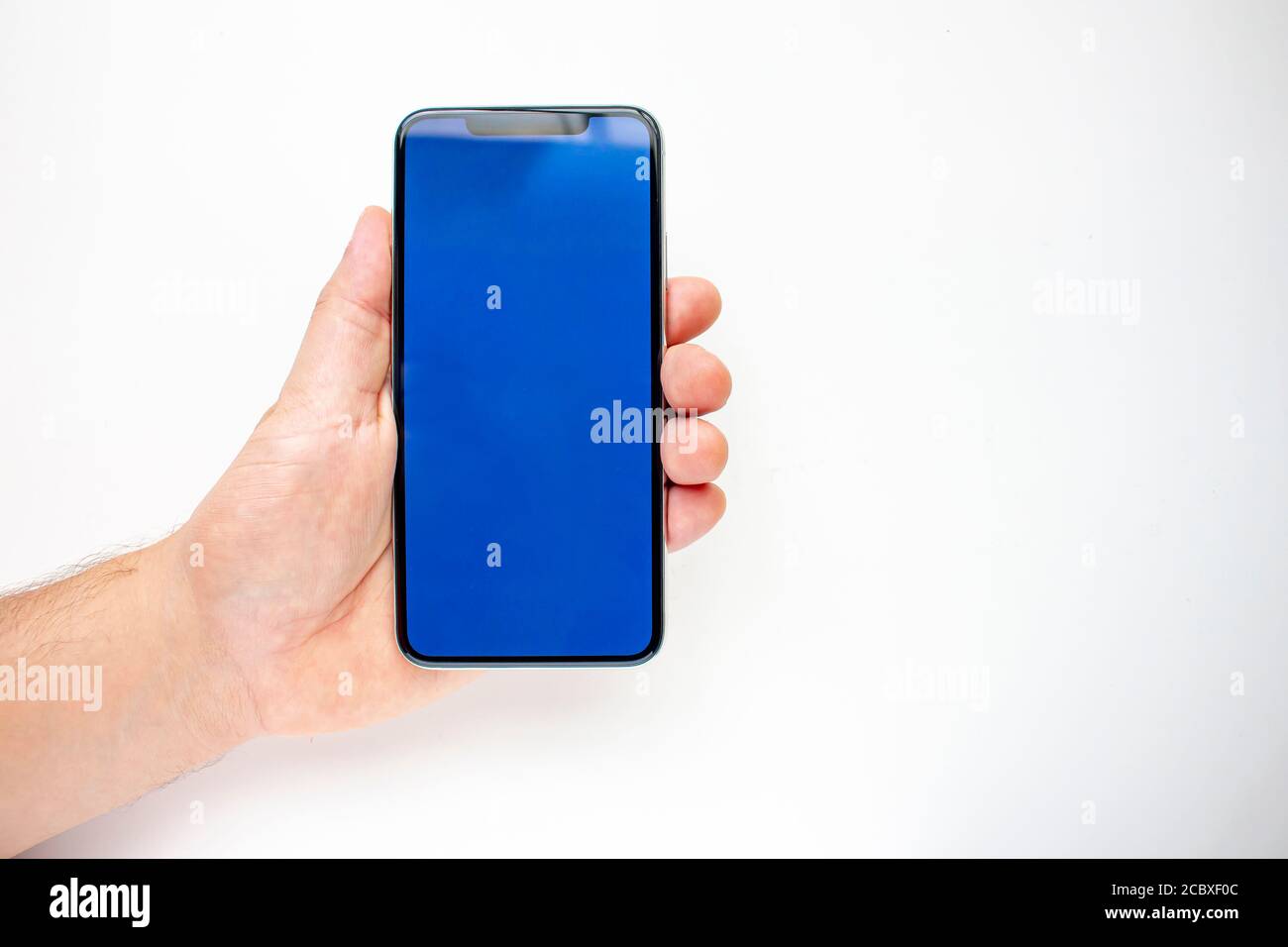 A person holding an Smart Phone with a blue screen on a white ...