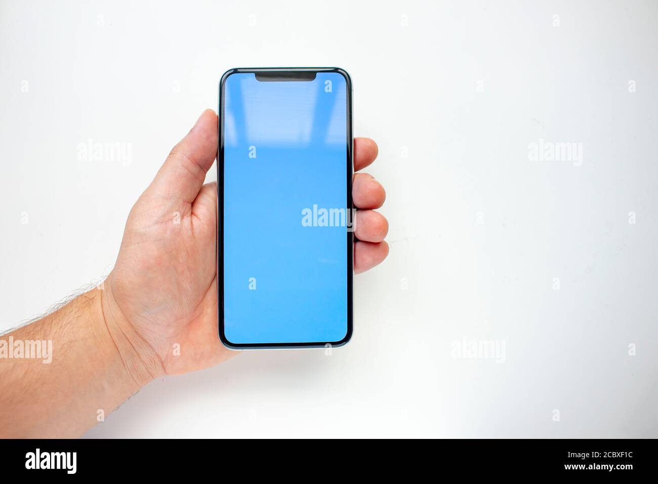 A person holding an Smart Phone with a blue sky screen on a white ...