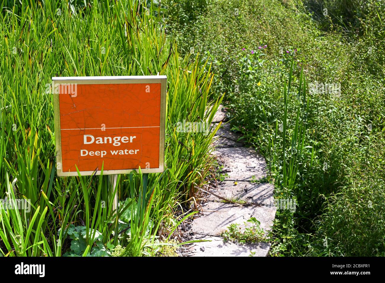 Sign warning of deep water alongside a path in landscaped garden Stock ...