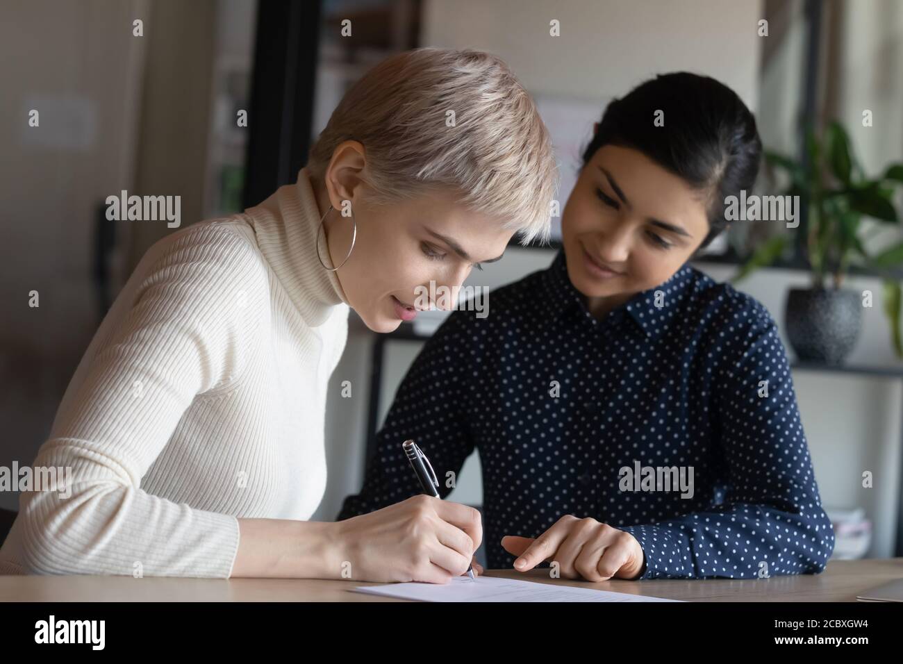 Smiling young indian manager showing place for signature to client ...