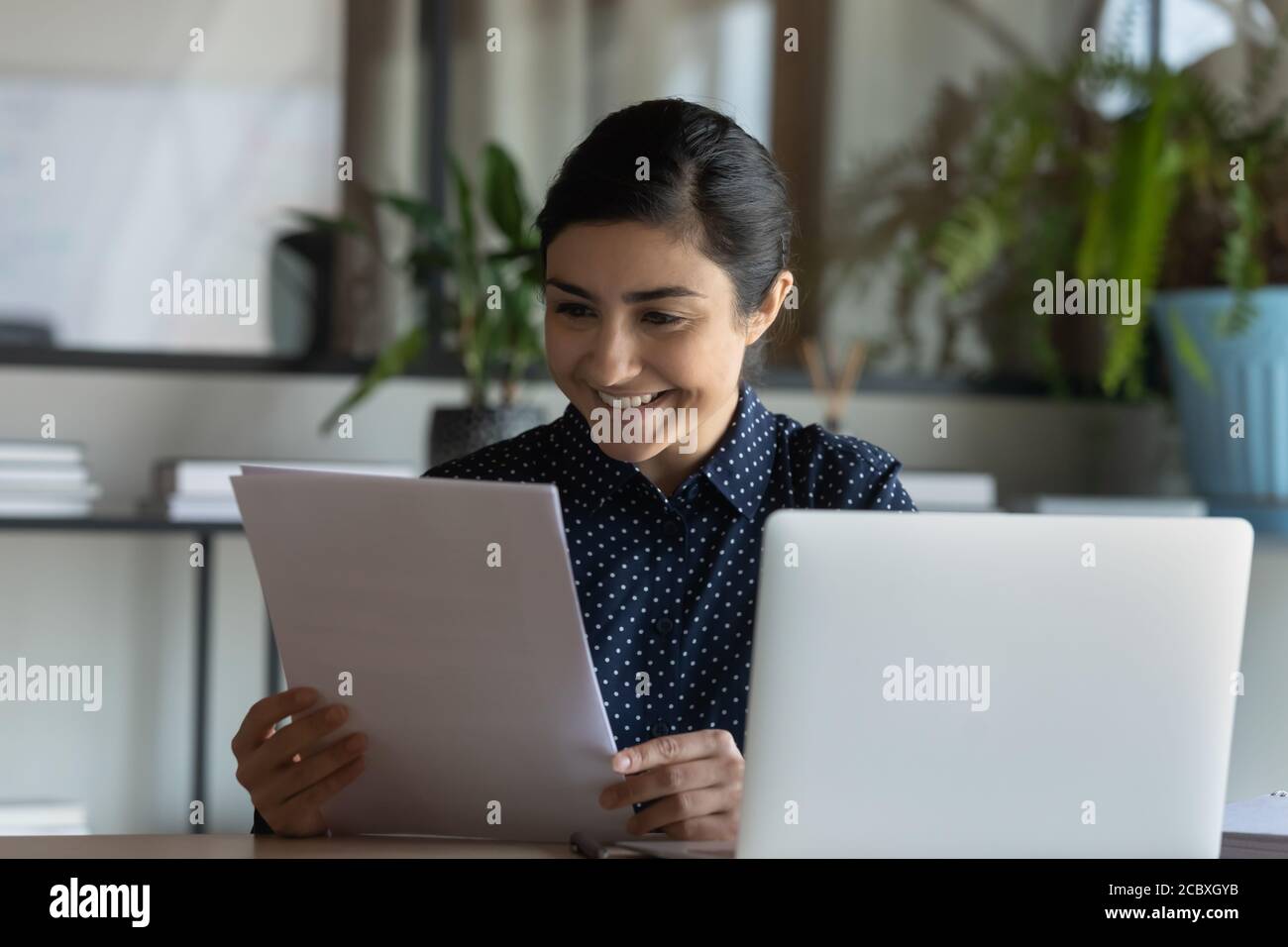 Happy young indian ethnicity female editor reading article on paper ...