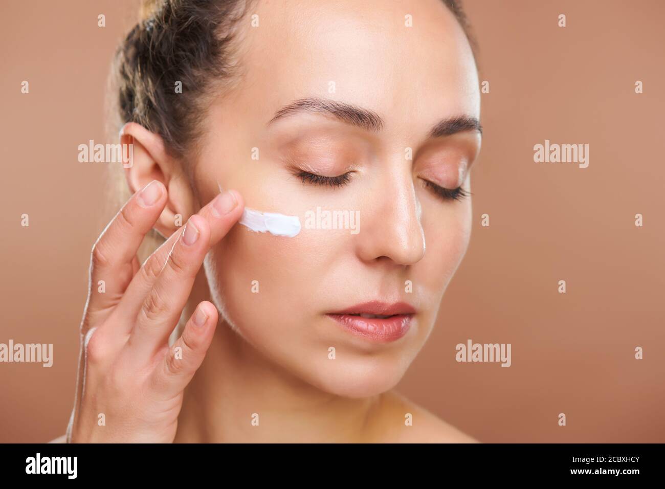 Young gorgeous female applying rejuvenating facial cream on undereye ...